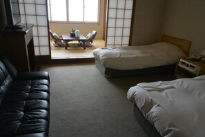 Quarto de hotel com cama, sofá e uma pequena mesa com cadeiras.