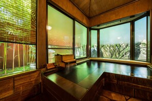 Uma onsen japonesa tradicional com bancos de madeira e amplas janelas com vista para uma floresta de bambu.