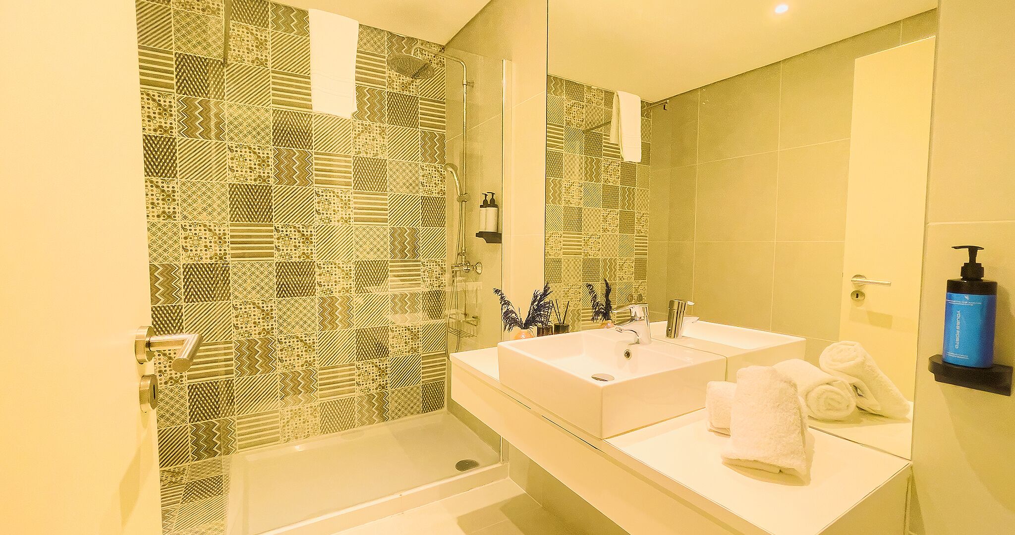 Casa de banho moderna com azulejos estampados, lavatório duplo, banheira e um espelho grande.