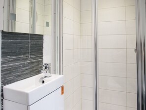 Um banheiro moderno com uma pia branca, toucador revestido de azulejos pretos e box de vidro.