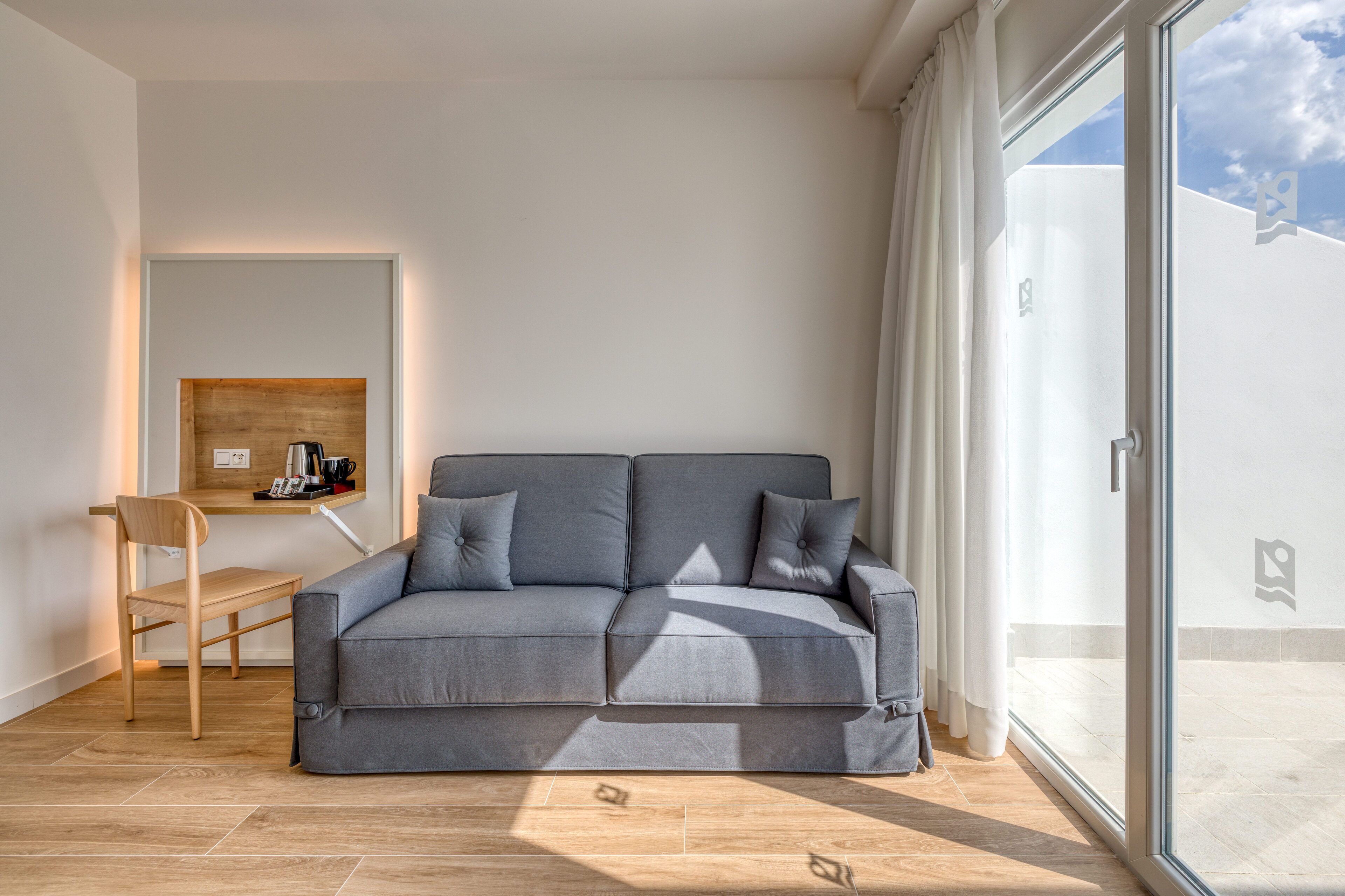 Uma sala de estar moderna com um sofá cinzento, uma cadeira de madeira e uma pequena mesa de madeira com uma máquina de café.