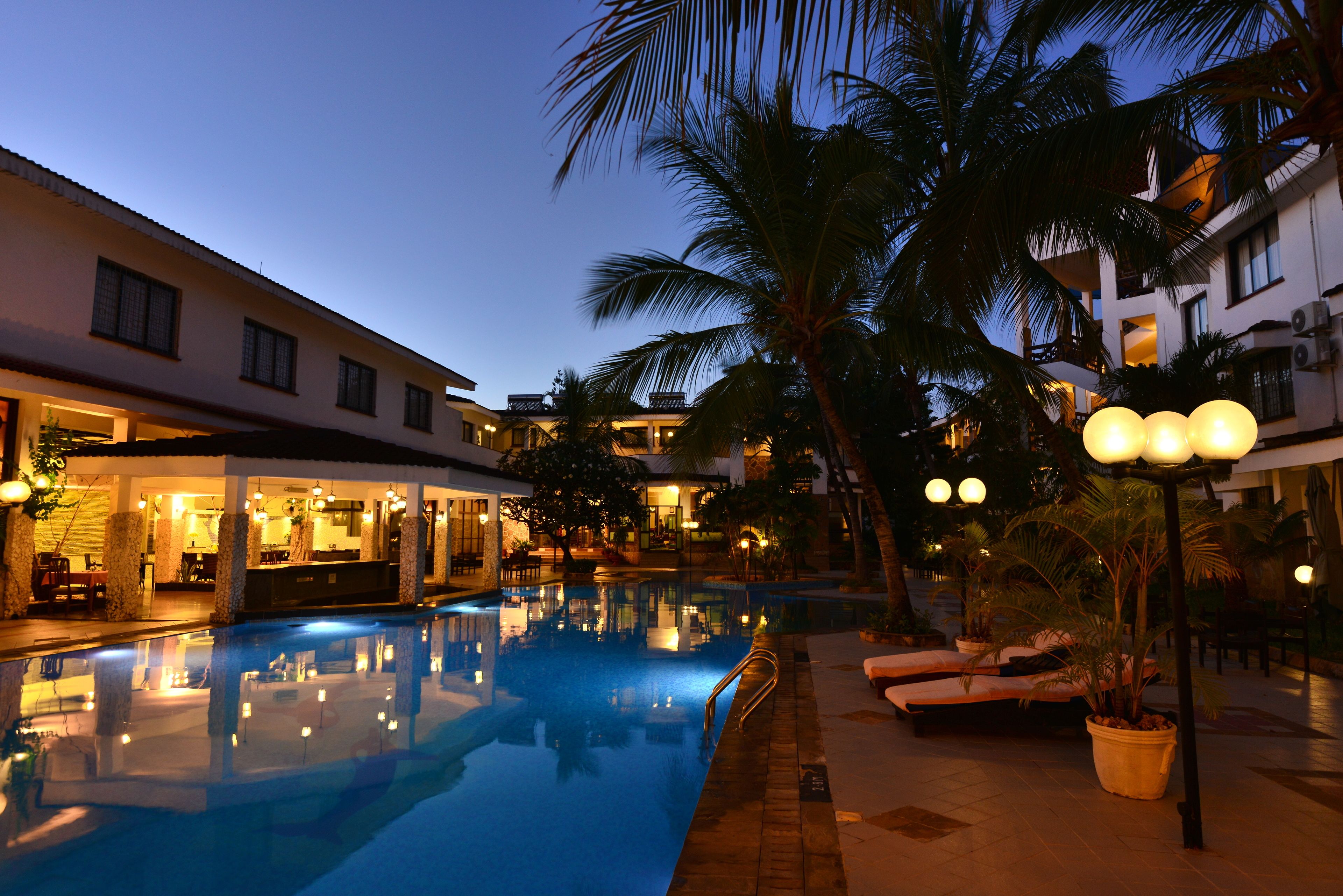 Piscina com espreguiçadeiras e palmeiras, cercada por edifícios com janelas iluminadas.
