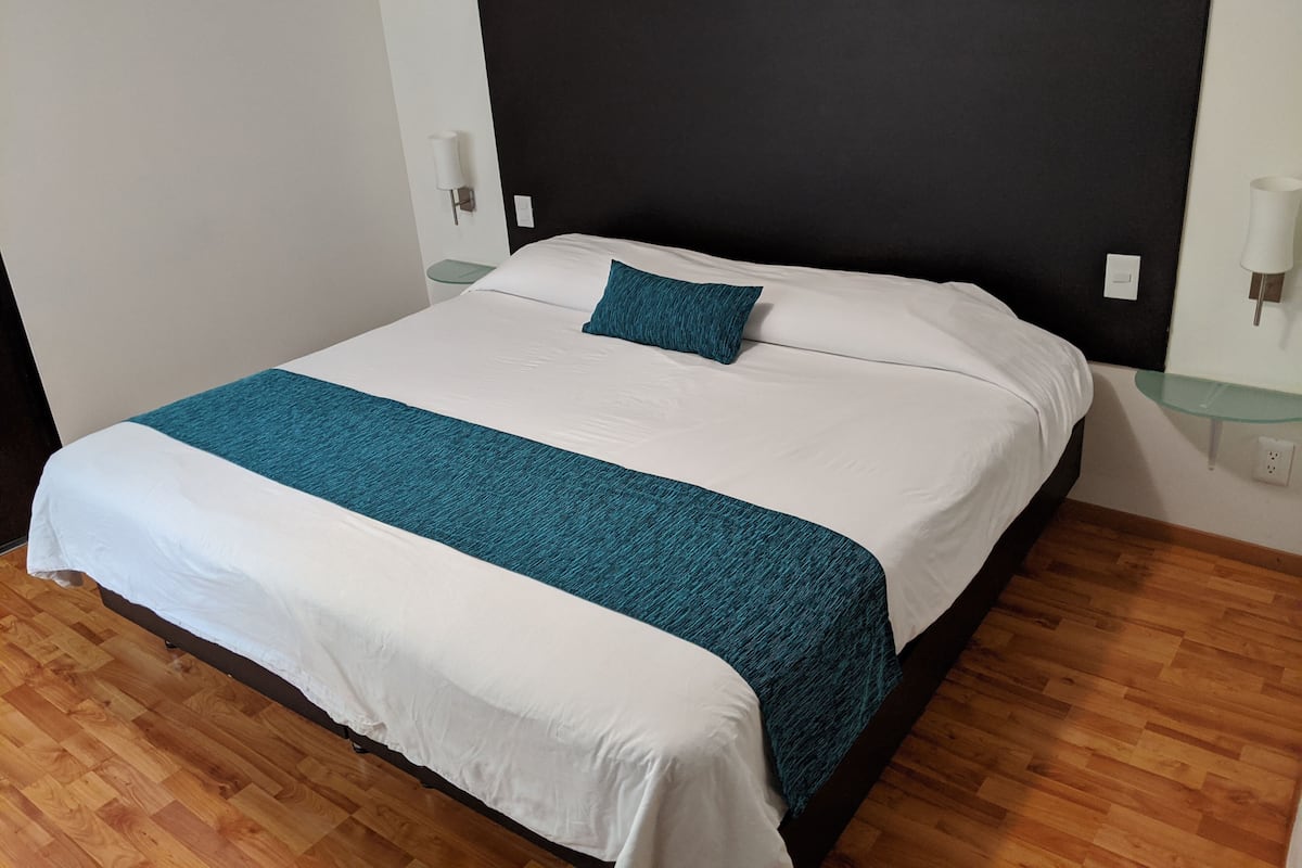Cama bem arrumada com colcha branca e azul-turquesa, travesseiro azul-turquesa e cabeceira preta.