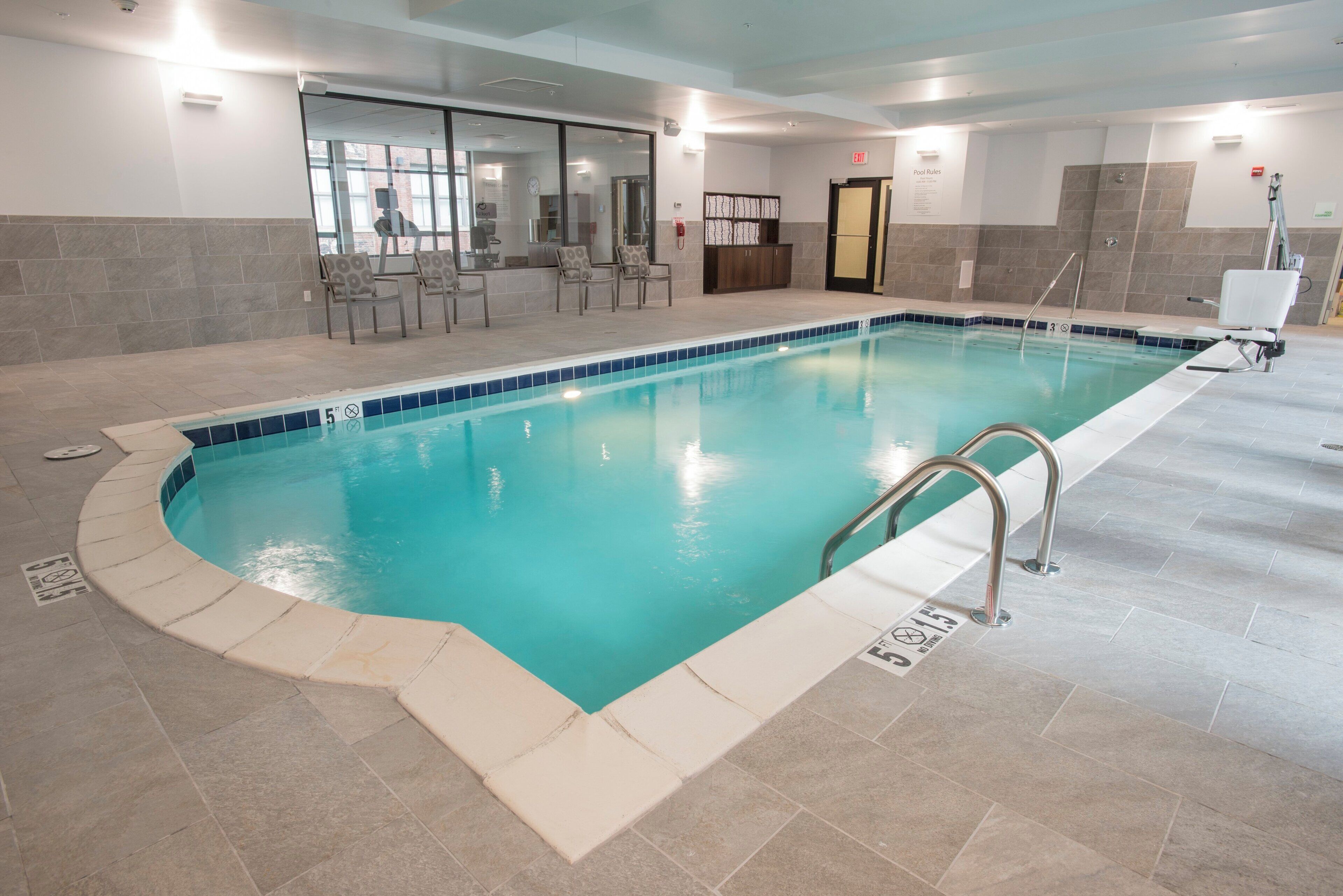 Piscina interior com água cristalina, cadeira de salva-vidas e área de descanso com cadeiras.