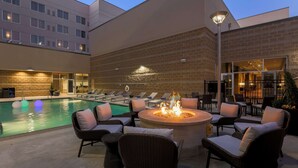 Uma área de piscina ao ar livre com espreguiçadeiras, lareira e um edifício com paredes de tijolo e janelas.