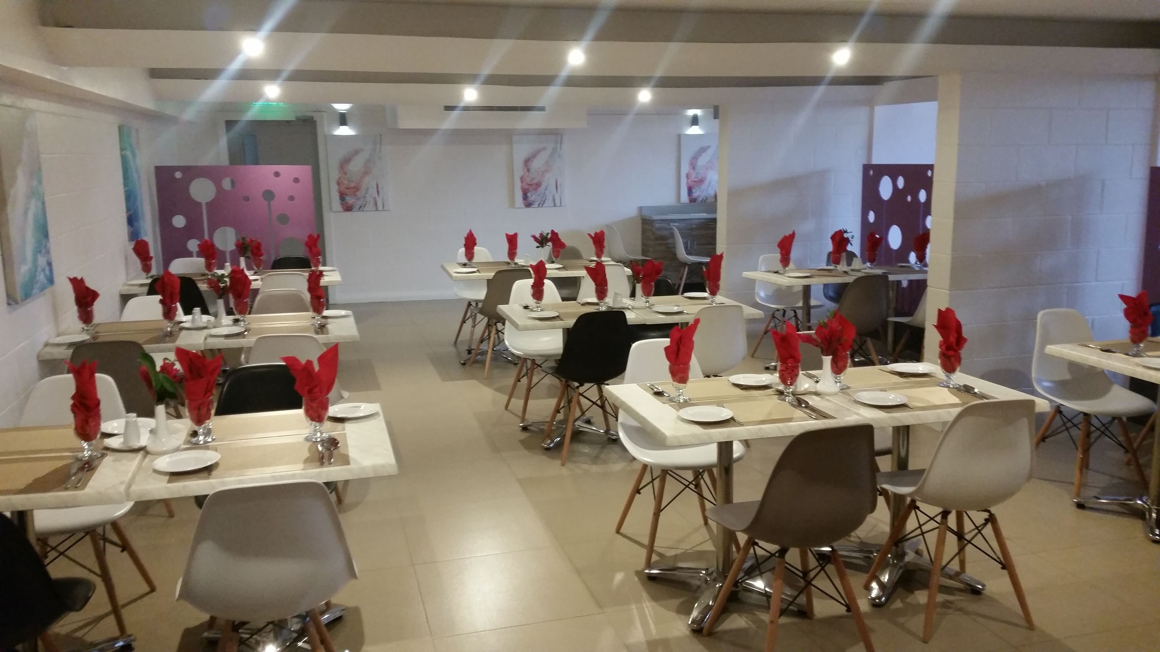 Uma sala de jantar com mesas preparadas para o serviço, cadeiras e obras de arte nas paredes.