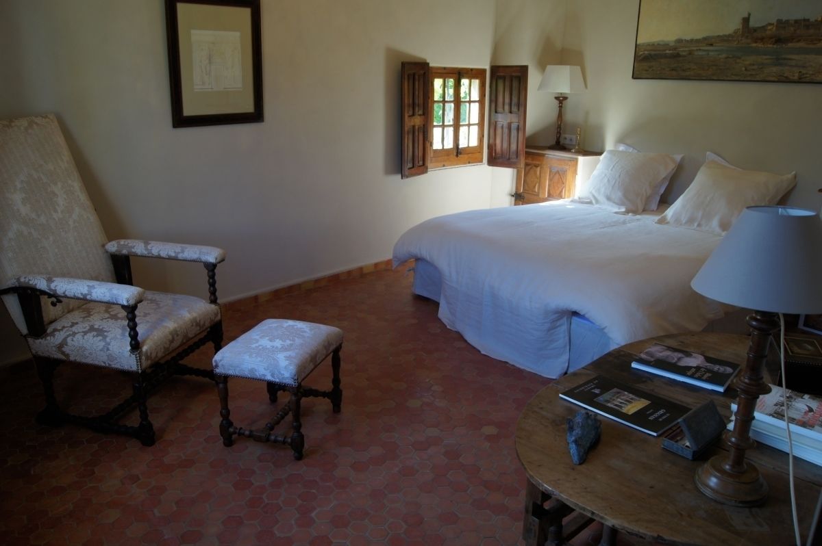 Um quarto com uma cama, uma cadeira, uma mesinha e um abajur.
