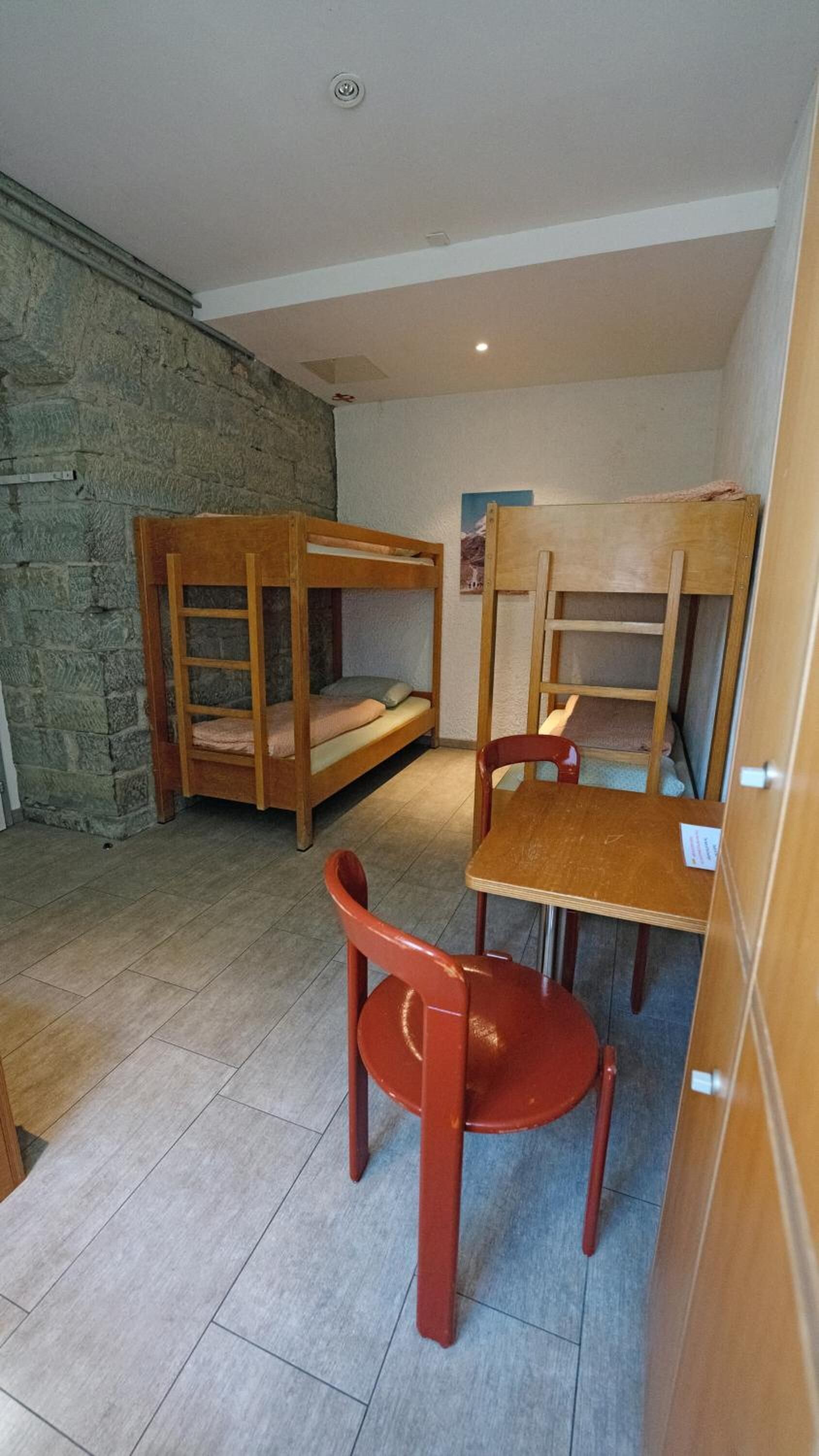 Quarto com beliches, uma mesa de madeira e uma cadeira vermelha.