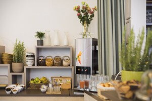 Um balcão de café da manhã com diversas opções de alimentos, uma máquina de café e plantas decorativas.