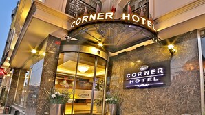 Exterior do Hotel Corner, com fachada de mármore, entrada de vidro e uma placa sobre a porta.