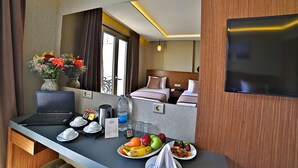 Quarto de hotel com escrivaninha, laptop, bandeja de café da manhã e cama com cabeceira.