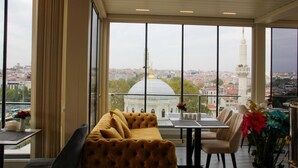 Quarto de hotel moderno com uma grande janela que oferece vista para uma paisagem urbana e um edifício branco de destaque com uma cúpula.