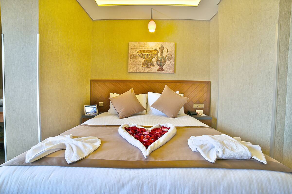 Quarto de hotel com cama bem arrumada, um quadro na parede e uma mesa pequena com abajur.