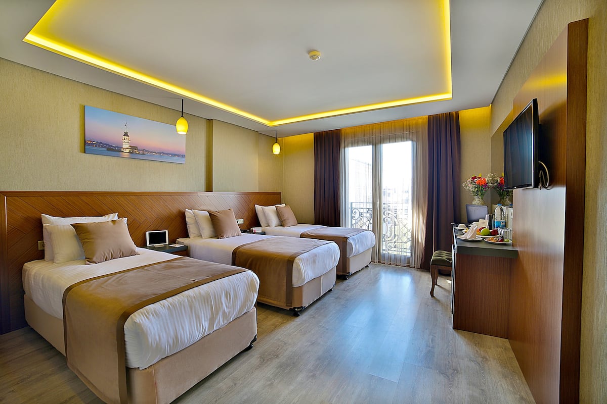 Quarto de hotel com duas camas, televisão, escrivaninha com cadeira e janela com cortinas.