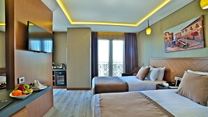 Quarto de hotel com duas camas, uma televisão de tela plana, uma escrivaninha com um laptop e um quadro na parede.