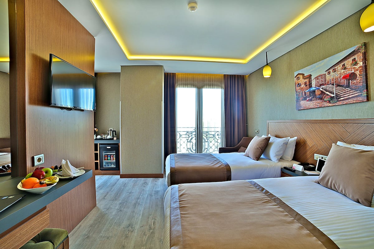 Quarto de hotel com duas camas, uma televisão de tela plana, uma escrivaninha com um laptop e um quadro na parede.