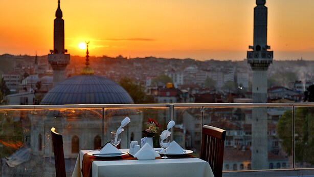 Mesa posta para dois com vista para um horizonte urbano ao pôr do sol, incluindo duas torres imponentes e uma cúpula.