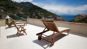 Duas poltronas de madeira num terraço com vista para uma vila costeira e montanhas.