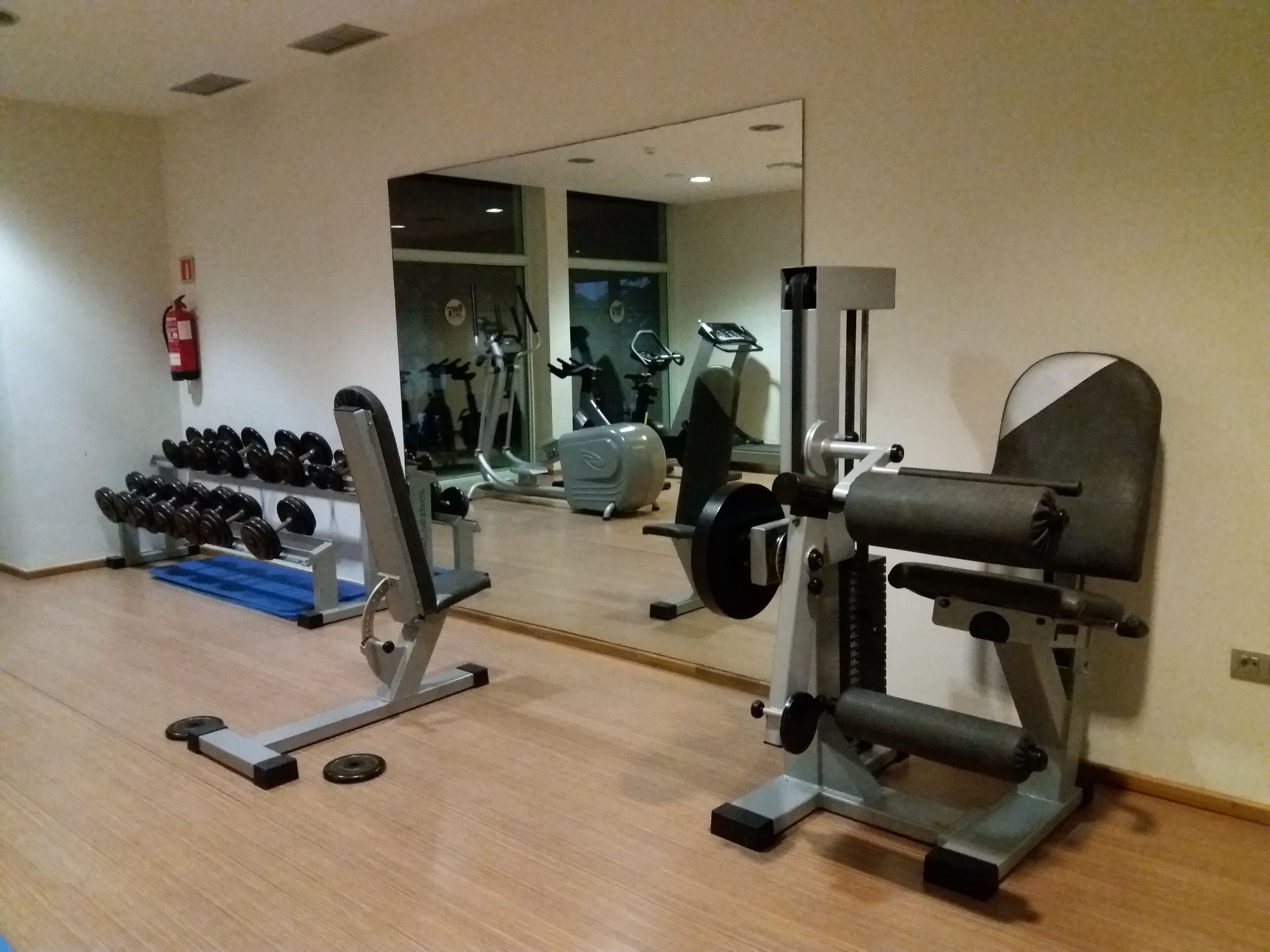 Uma academia com equipamentos de exercício, um espelho e uma fileira de halteres.