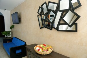 Quarto com sofá azul, cesta de frutas sobre mesa de madeira e parede decorada com vários espelhos.