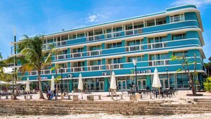 Um hotel de vários andares com fachada azul e branca, área de estar ao ar livre e palmeiras.