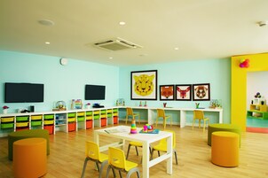Uma sala de brinquedos infantil, vibrante, com uma mesa branca, cadeiras amarelas e unidades de armazenamento coloridas.