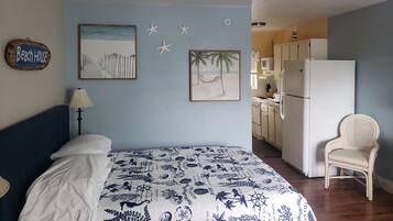 Quarto com cama, ventilador de teto e uma obra de arte na parede retratando uma praia.