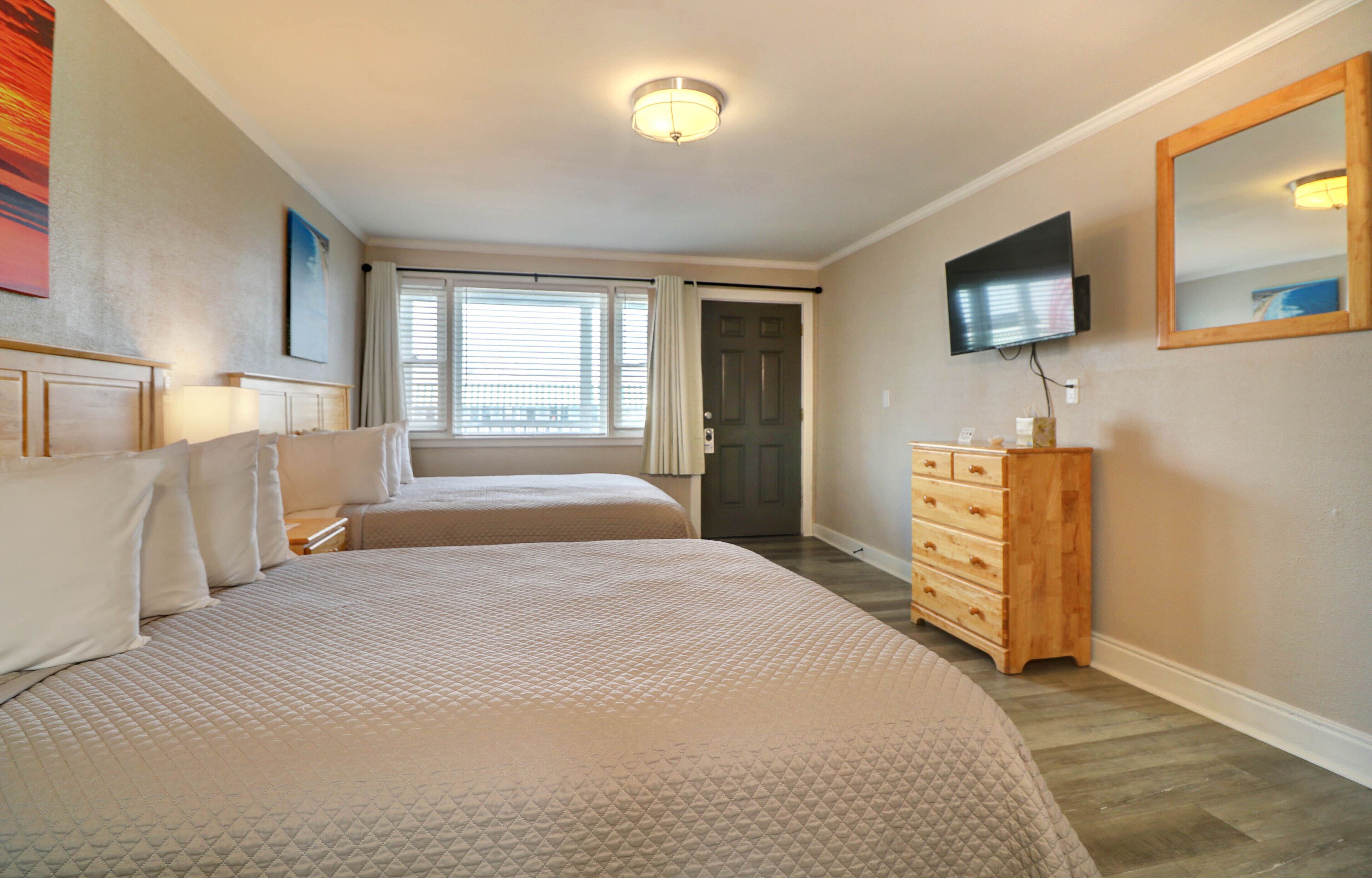 Quarto de hotel com duas camas, uma cômoda, uma televisão e uma porta.