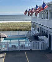 Área da piscina com vista para o oceano, cercada por uma cerca branca e bandeiras americanas.