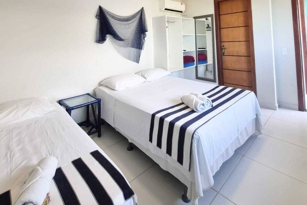 Quarto de hotel com duas camas, uma mesinha, um espelho e uma porta.