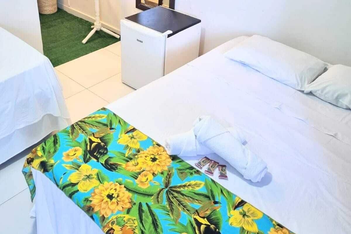 Quarto de hotel com duas camas, um guarda-roupa, um espelho e uma pequena mesa branca.