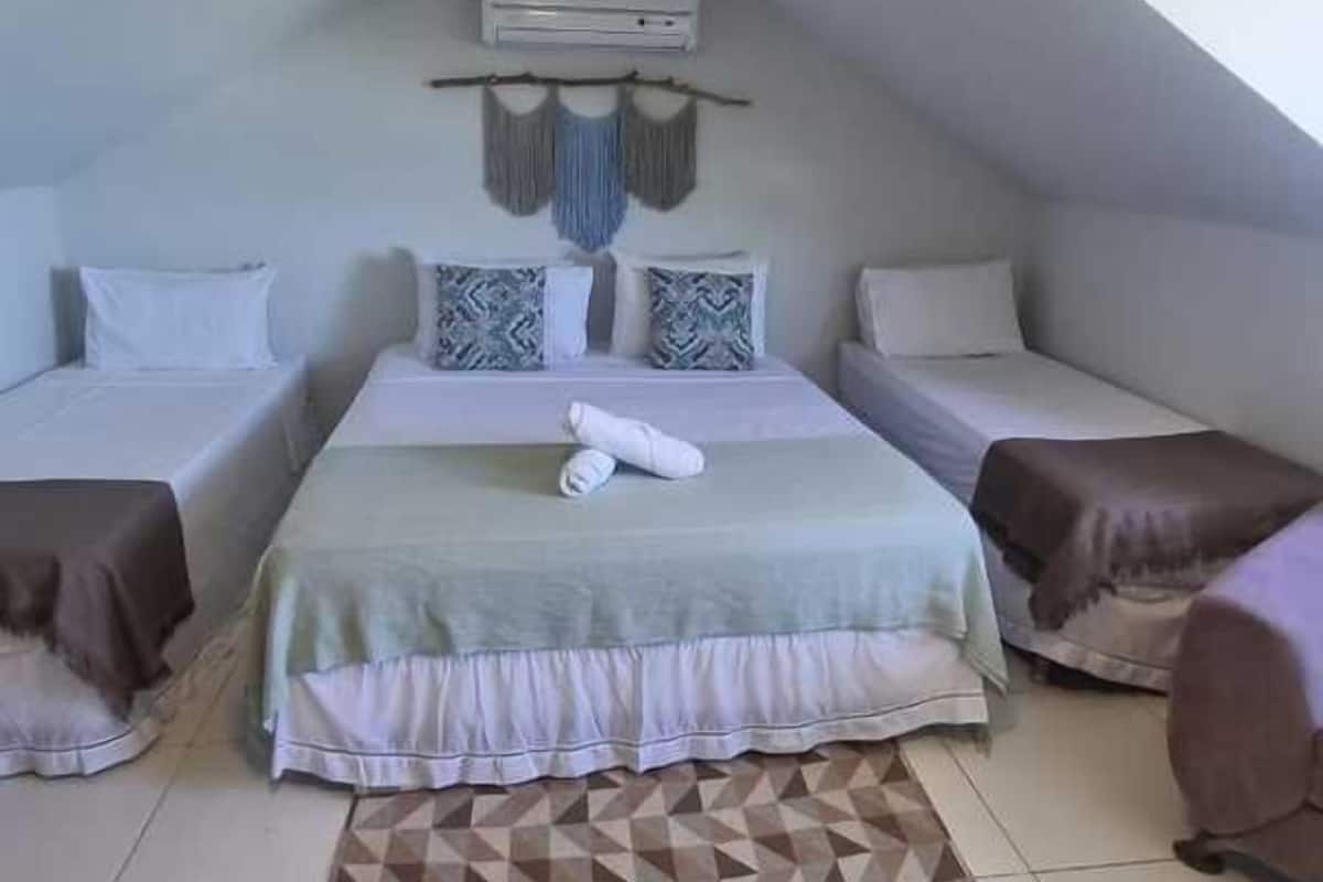 Um quarto acolhedor em formato triangular, com duas camas, um tapete estampado e um teto com detalhes de folhas.