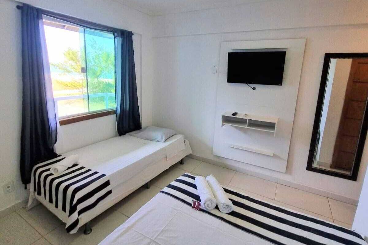 Quarto de hotel com cama, sofá-cama, televisão e janela com cortinas.