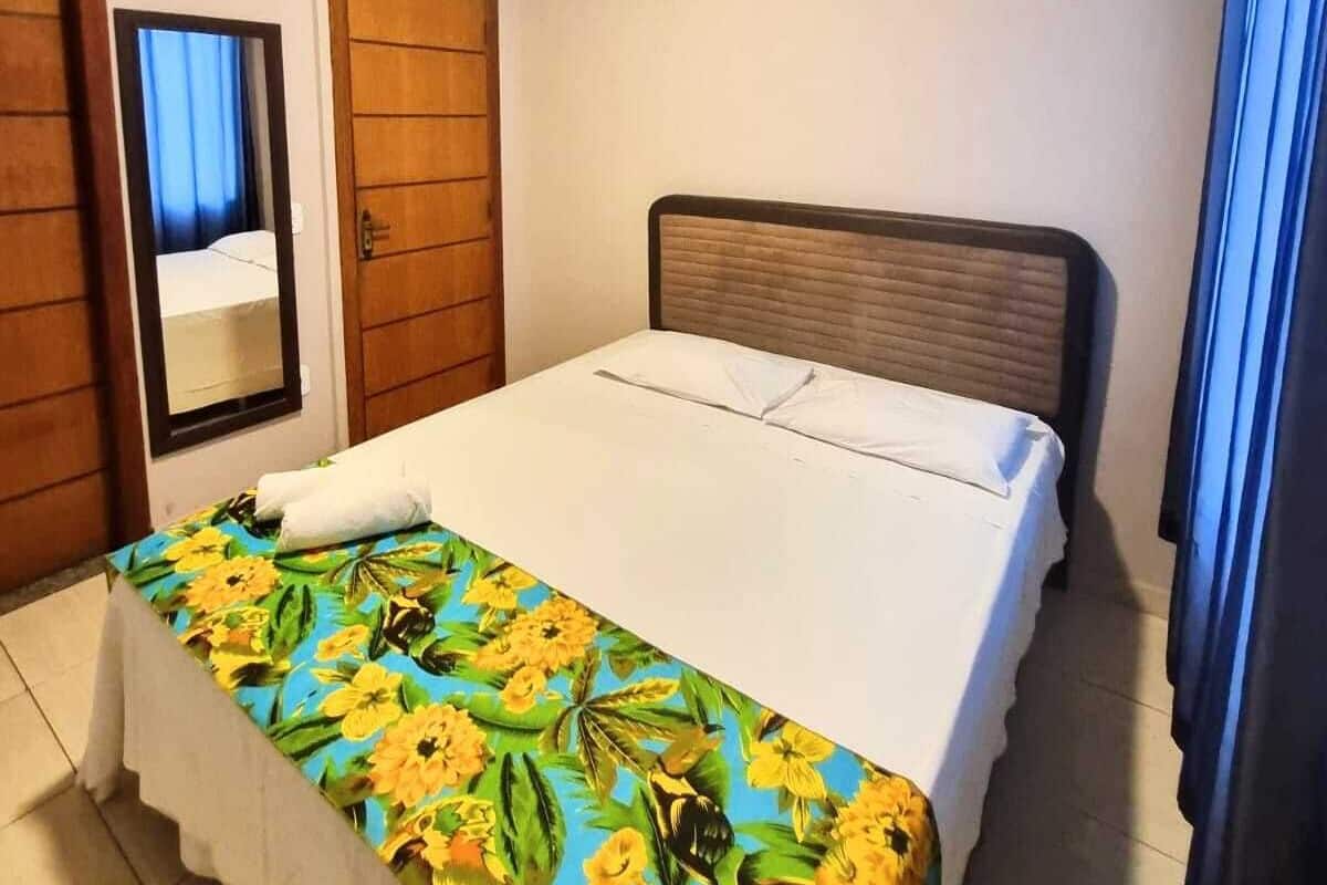 Quarto com cama, guarda-roupa, espelho e janela com cortinas.
