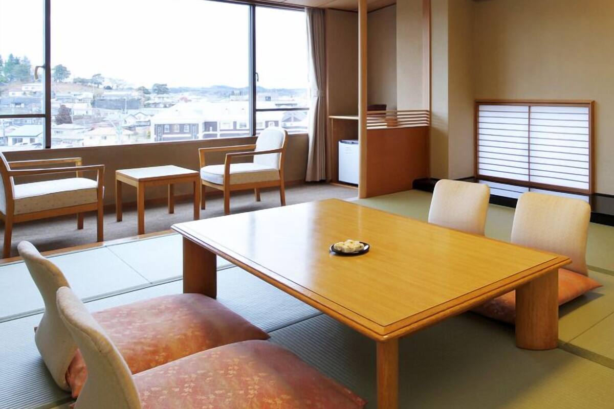 Quarto com uma grande janela, uma mesa de madeira e disposição de assentos.