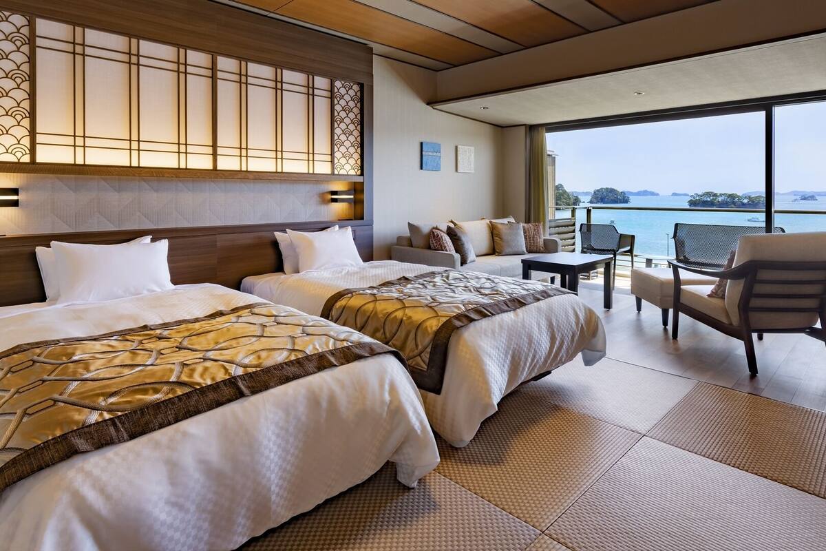 Quarto de hotel com duas camas, um sofá, uma mesa e vista para o mar.