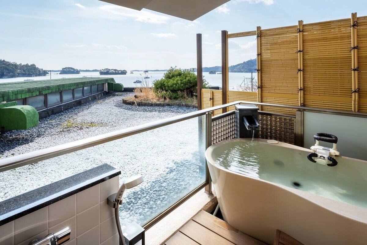 Uma varanda com vista para um corpo de água, uma banheira de hidromassagem e um biombo de bambu.