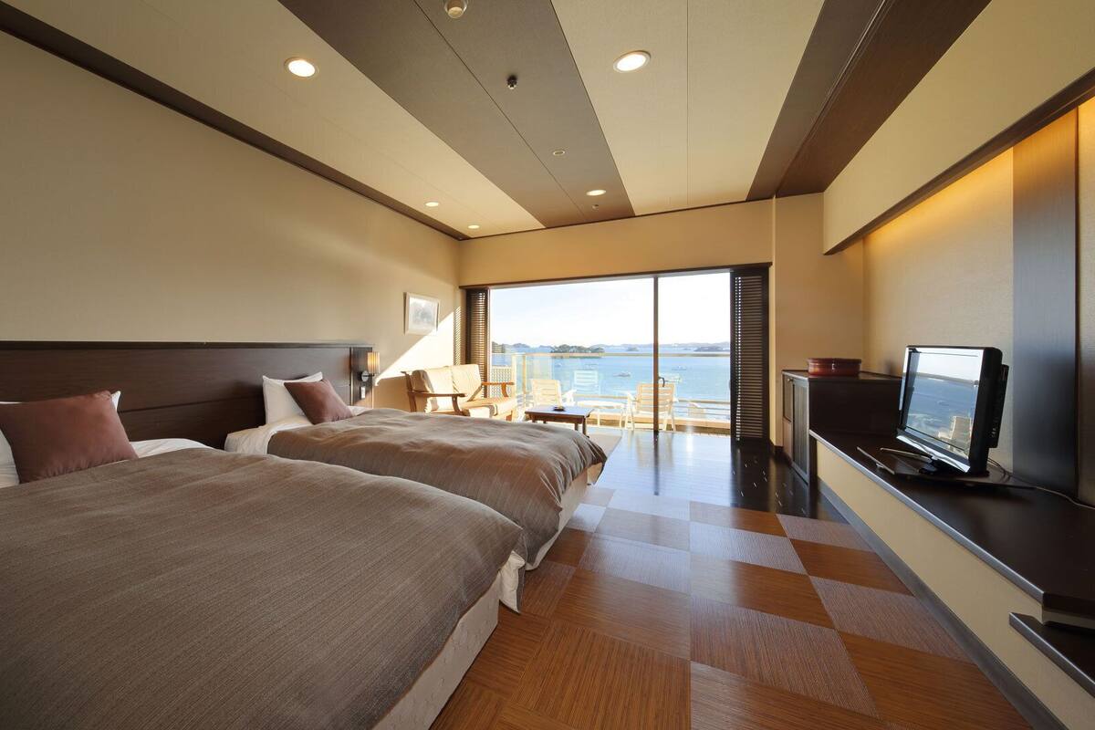 Quarto de hotel com duas camas, televisão e vista para o mar.