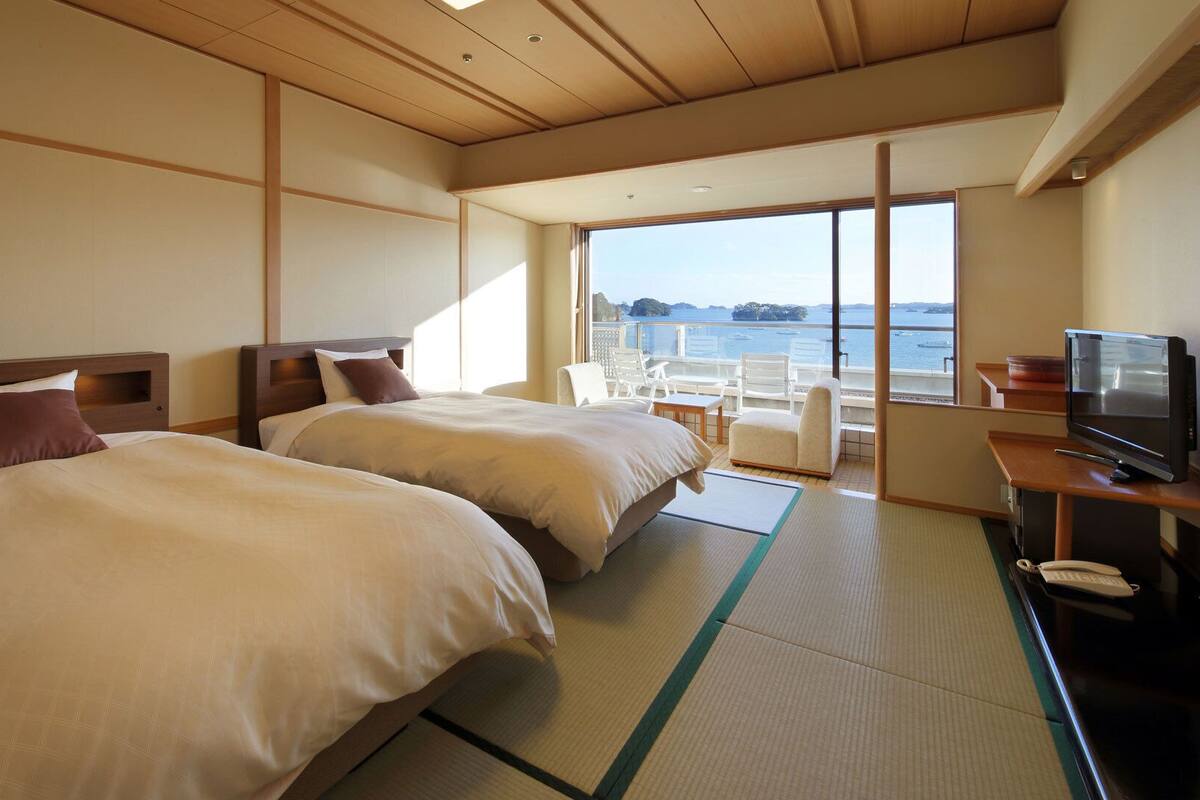 Quarto de hotel com duas camas, televisão e vista para o mar.