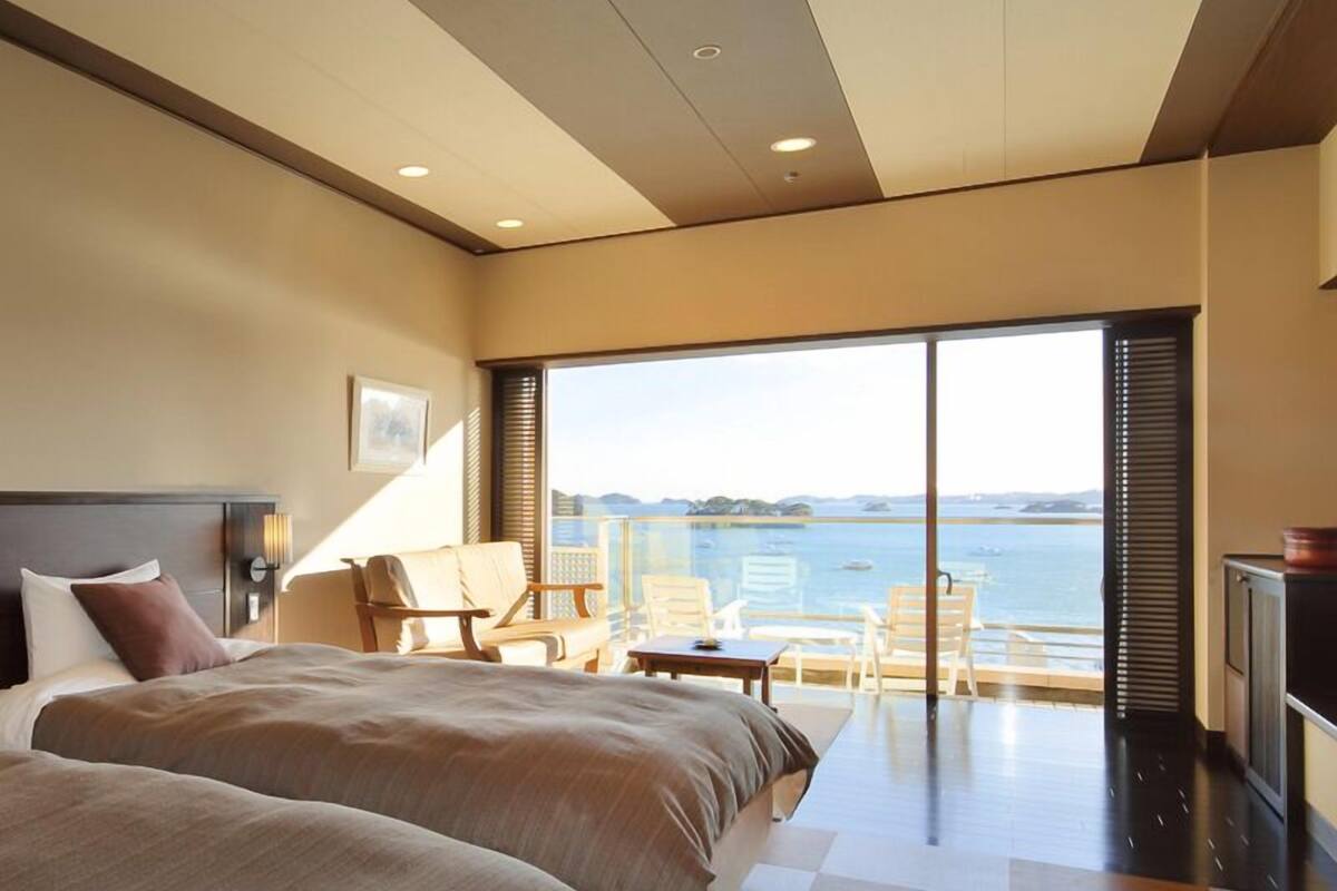 Quarto de hotel moderno com duas camas, varanda com vista para o mar e uma janela ampla.
