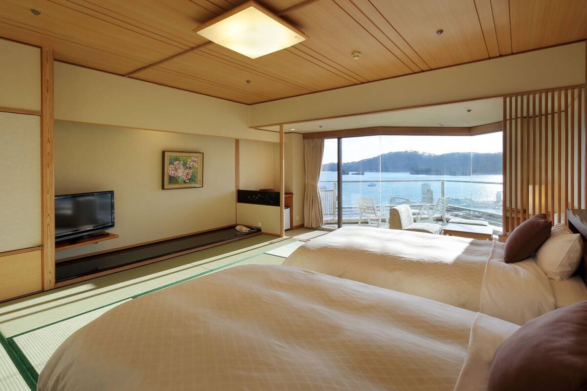 Quarto de hotel com uma cama grande, televisão, pintura e vista para um corpo de água.