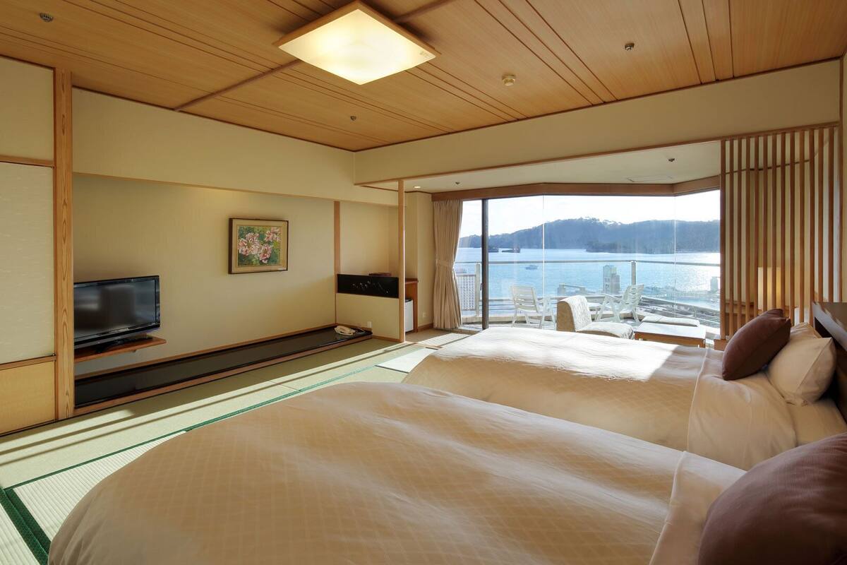 Quarto de hotel com uma cama grande, televisão, pintura e vista para a água.