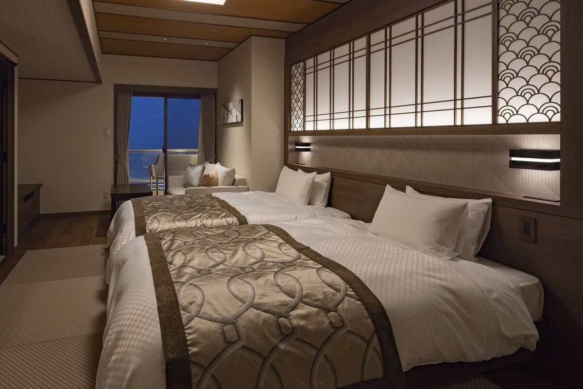 Quarto de hotel com uma cama grande, uma mesa, uma cadeira e vista para o exterior.