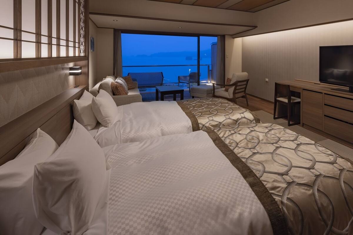 Quarto de hotel com duas camas, televisão, escrivaninha e varanda com vista.