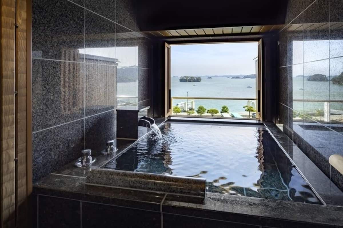 Área de spa com vista para o mar, uma banheira de hidromassagem e um painel de parede de madeira.