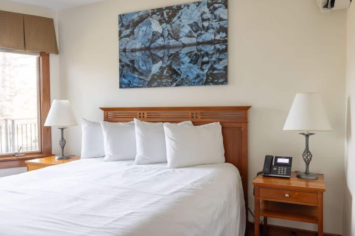 Quarto de hotel com uma cama grande, duas mesas de cabeceira com luminárias, um telefone e um quadro na parede.