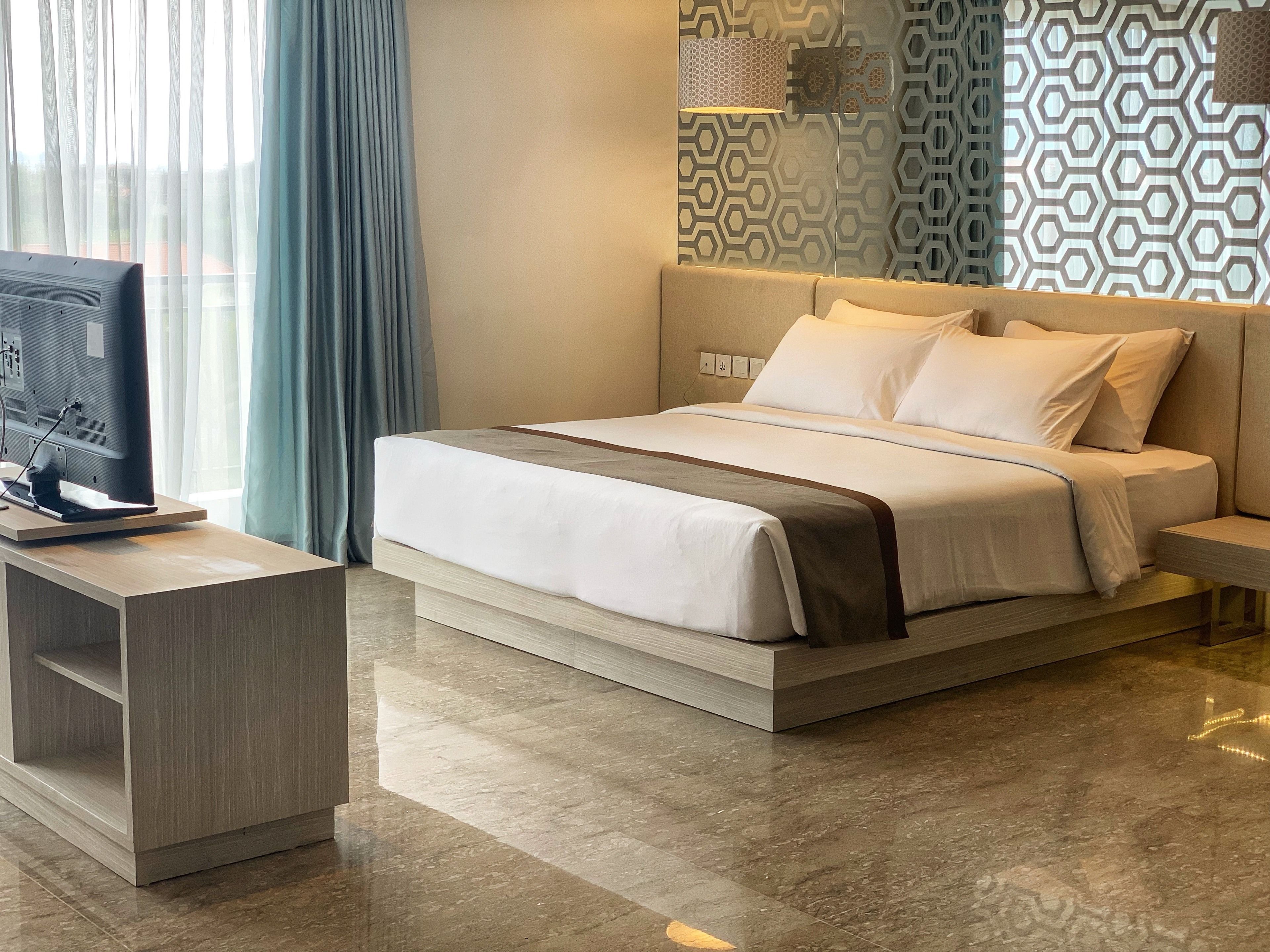Quarto de hotel moderno com uma cama grande, uma escrivaninha com computador e uma parede estampada.