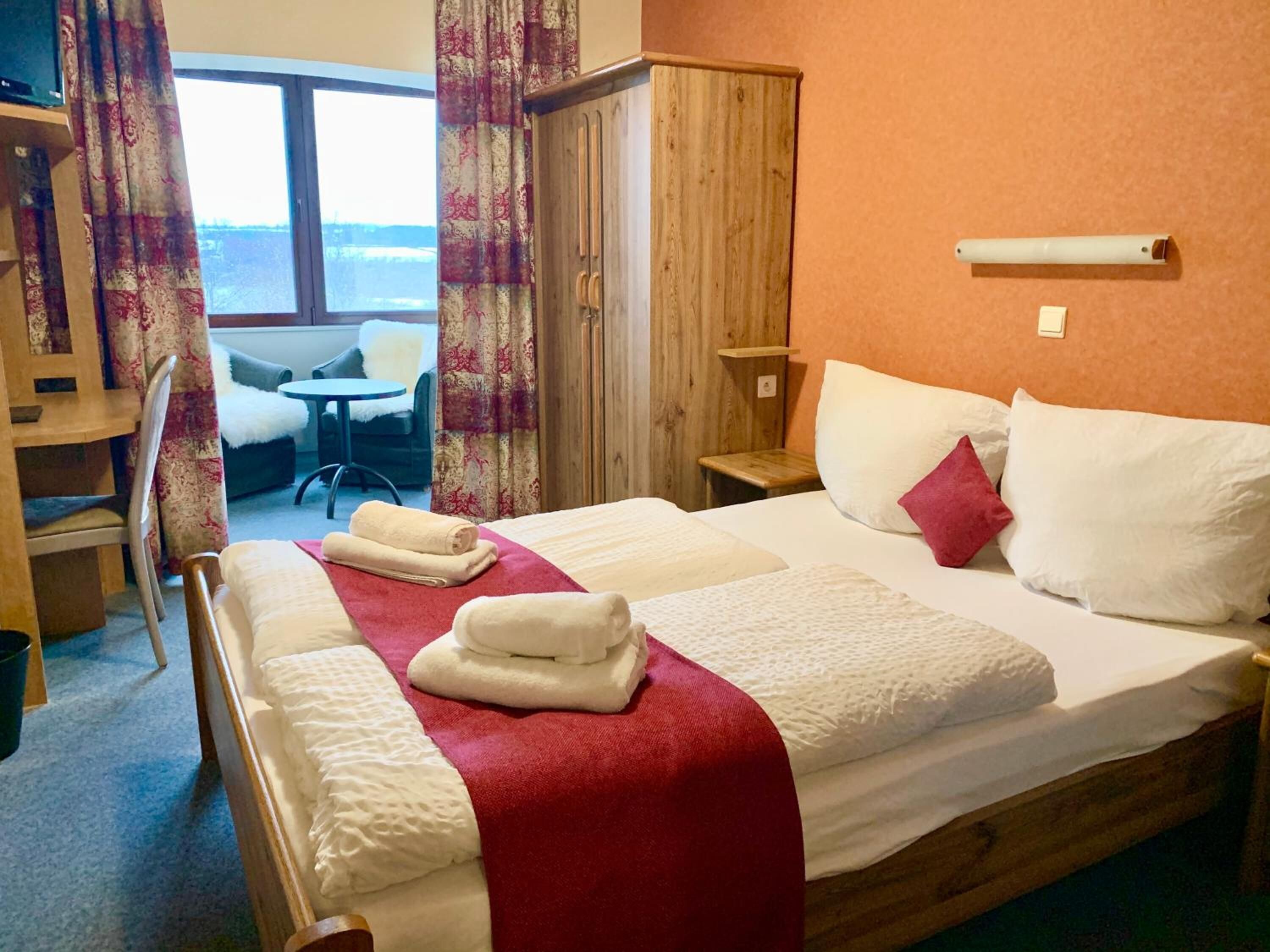 Quarto de hotel com cama, guarda-roupa de madeira, secretária e uma cadeira.