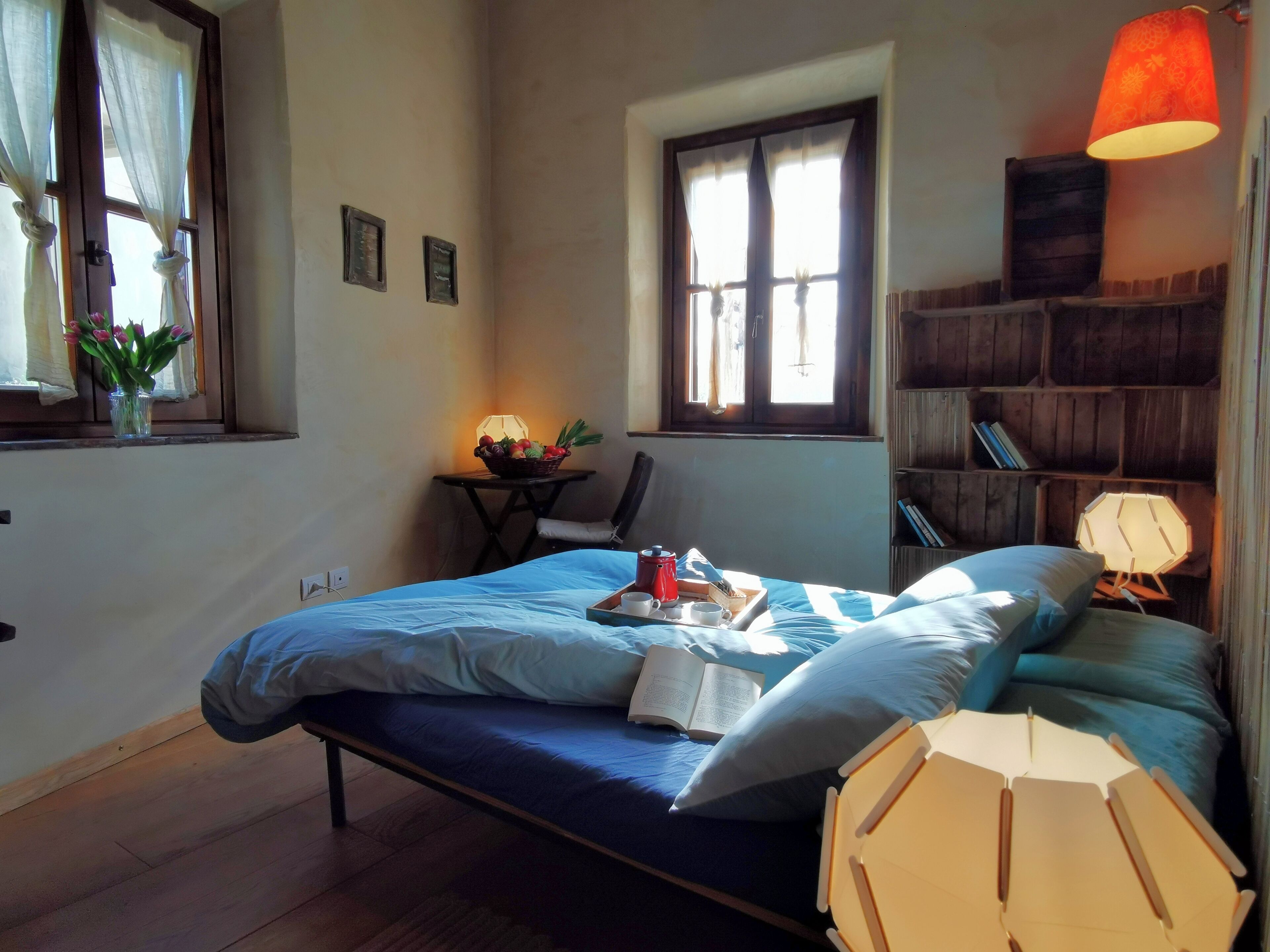 Quarto com cama, mesa de cabeceira, abajur, janela e estante de livros.
