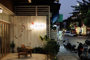 Restaurante chamado ASAYA com mesas ao ar livre, plantas em vasos e scooters estacionadas.